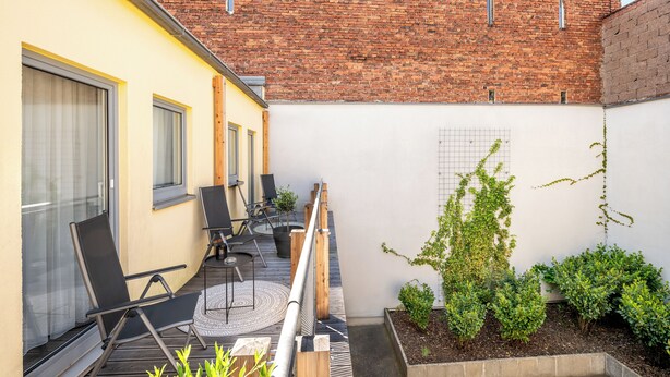 Uma varanda com mobiliário de exterior, um muro de tijolos e uma área ajardinada.