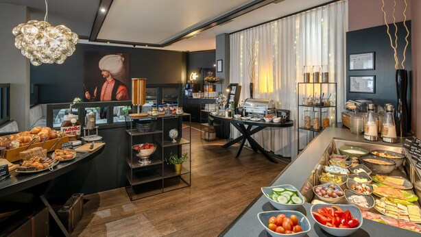 Quarto de hotel moderno com buffet de café da manhã, espaço para café e uma grande janela com cortinas.