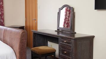 Quarto de hotel com uma escrivaninha de madeira, uma cadeira, uma cama e uma televisão fixada na parede.