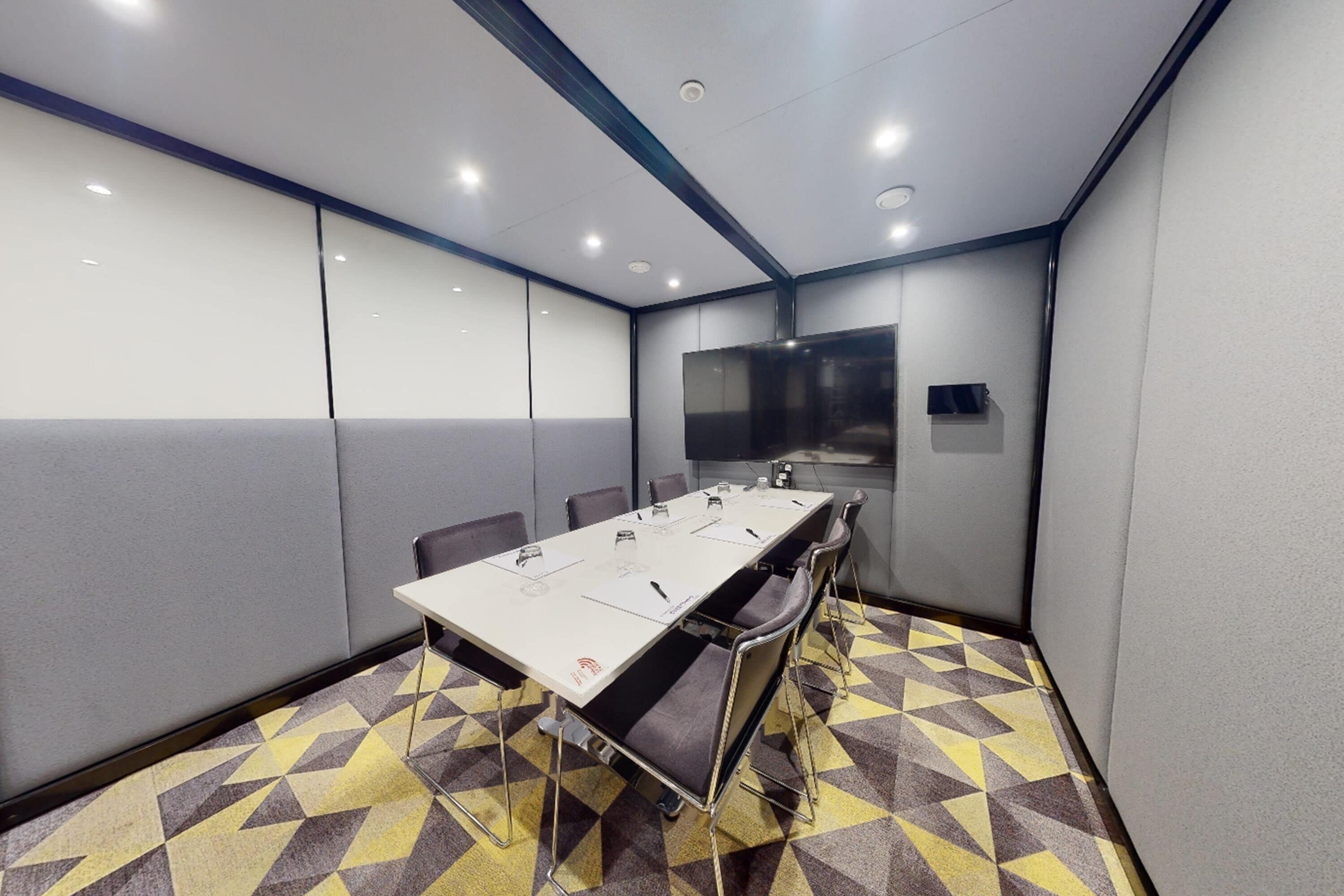 Uma sala de conferências com uma mesa comprida, cadeiras e uma tela de projeção.