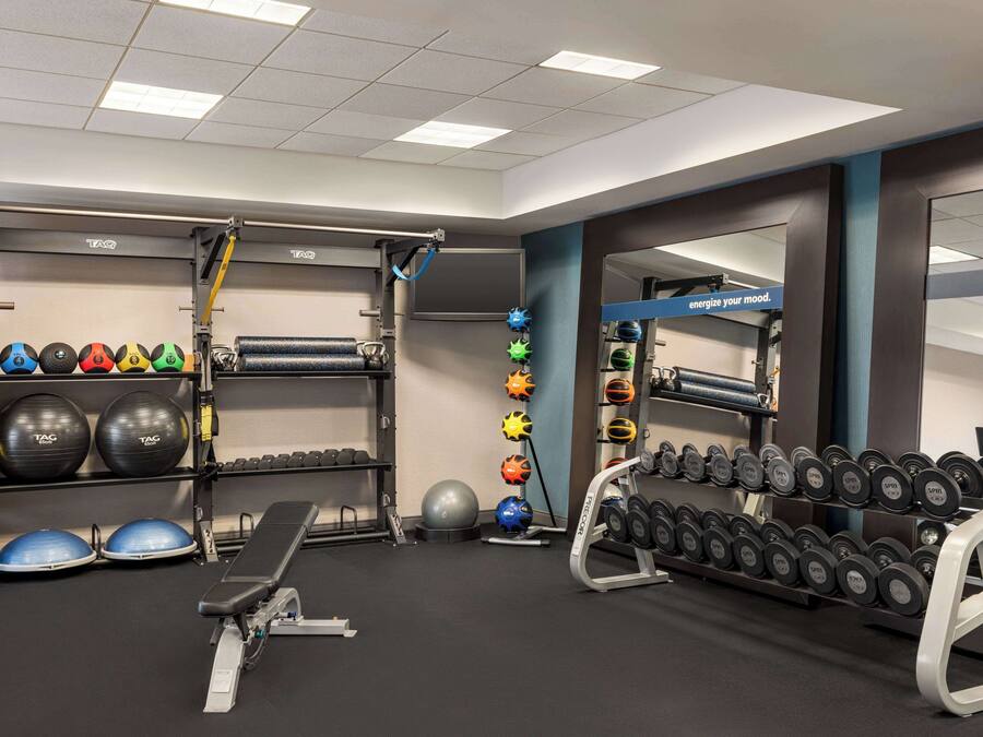 Uma academia com equipamentos de ginástica, incluindo halteres, bolas de medicina e um banco.