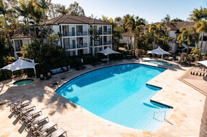 Um hotel com uma piscina grande, várias áreas de estar com guarda-sóis e um edifício com varandas.