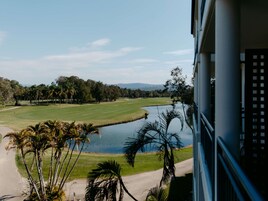 Vista de um campo de golfe com um corpo de água, palmeiras e um edifício em primeiro plano.