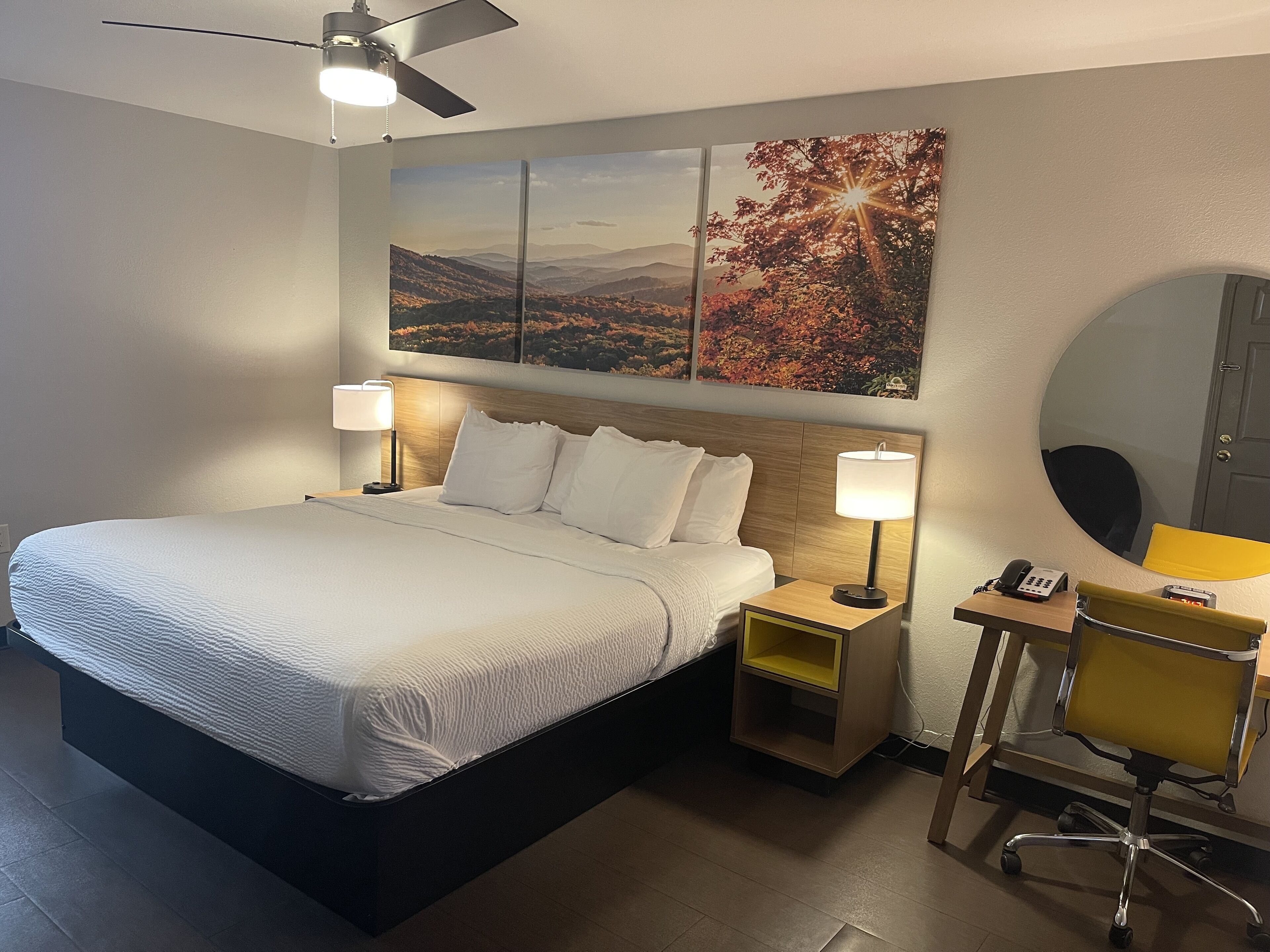 Quarto de hotel com cama, duas luminárias de cabeceira, escrivaninha com cadeira e um espelho grande.