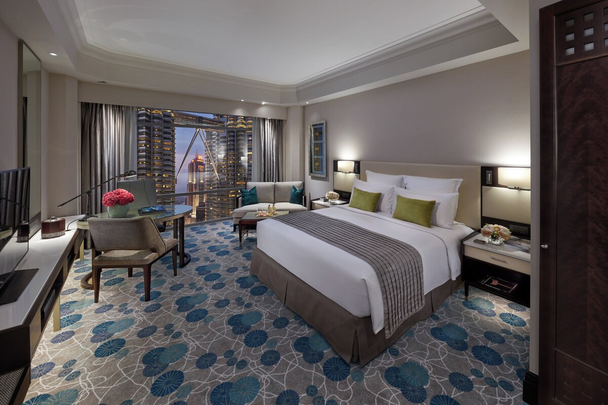 Quarto de hotel com uma cama grande, uma mesa, uma cadeira, uma televisão e vista para a paisagem urbana.