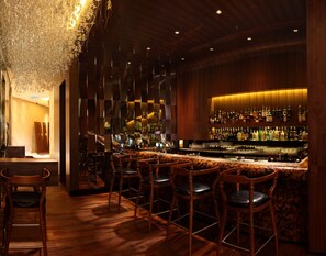 Uma área de bar com banquetas de madeira, uma prateleira de bebidas bem abastecida e um lustre decorativo.