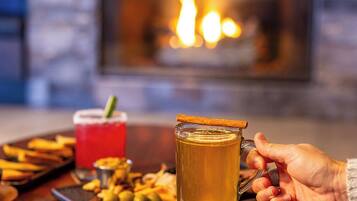 Uma área de refeições acolhedora com lareira, uma chávena de chá, um prato de comida e um cocktail.