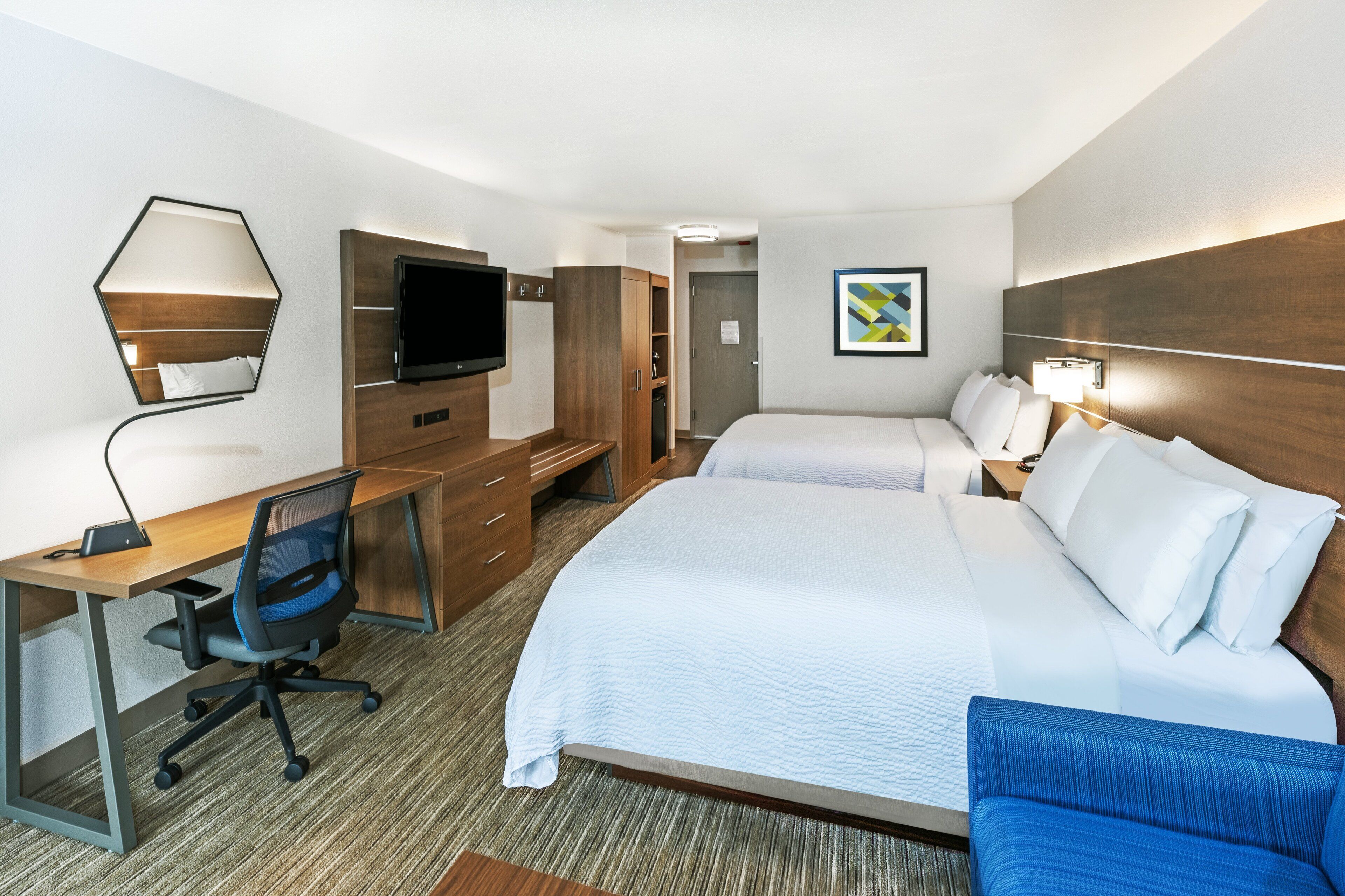 Quarto de hotel com cama, escrivaninha, cadeira, televisão e porta para o banheiro.
