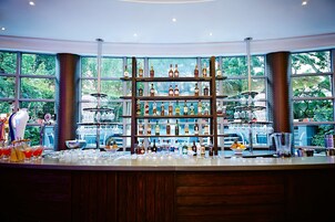 Uma área de bar com prateleiras cheias de garrafas de bebidas, copos e uma cesta de frutas.