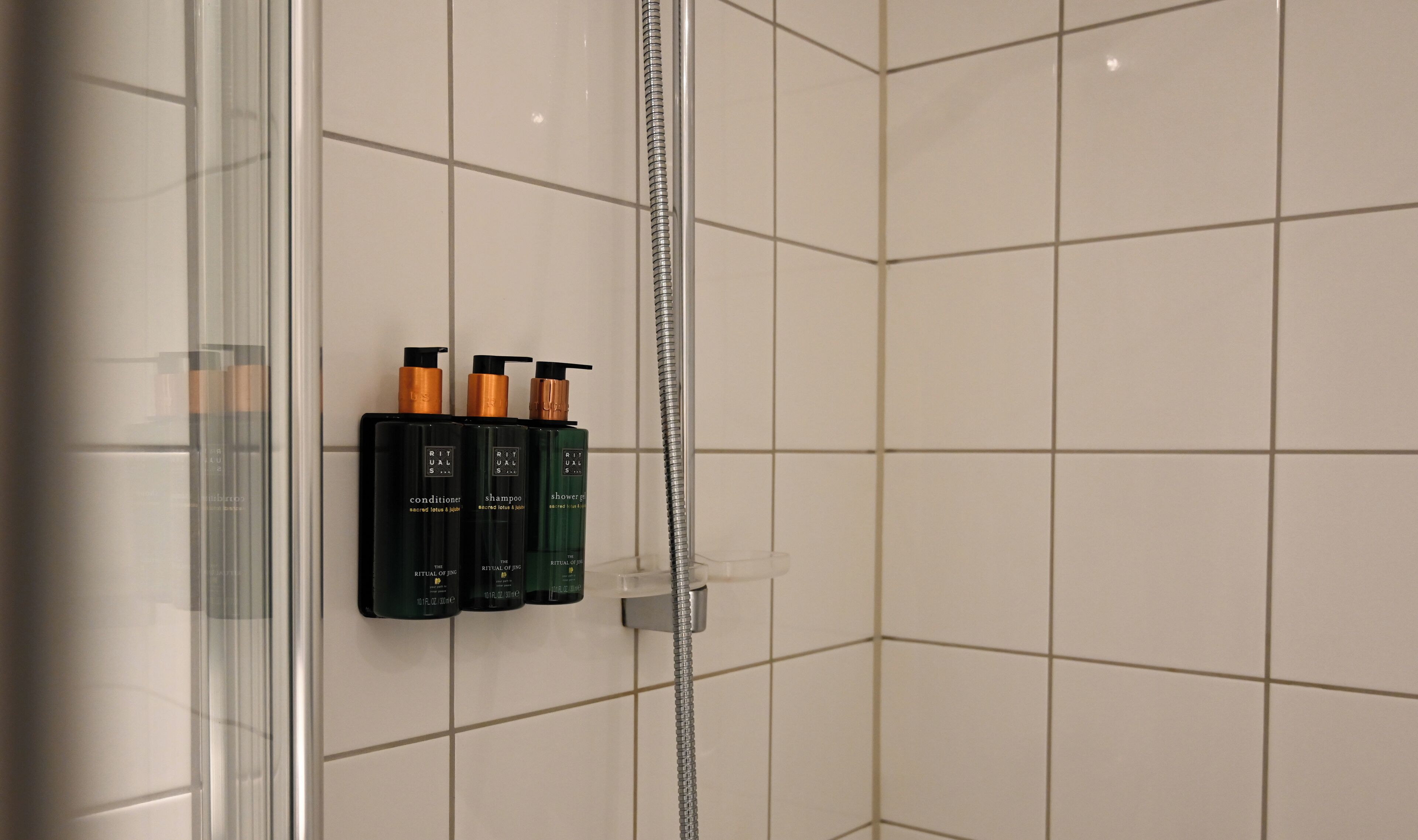 Um banheiro com box de vidro, paredes revestidas de azulejos brancos e um conjunto de produtos de higiene em uma prateleira.