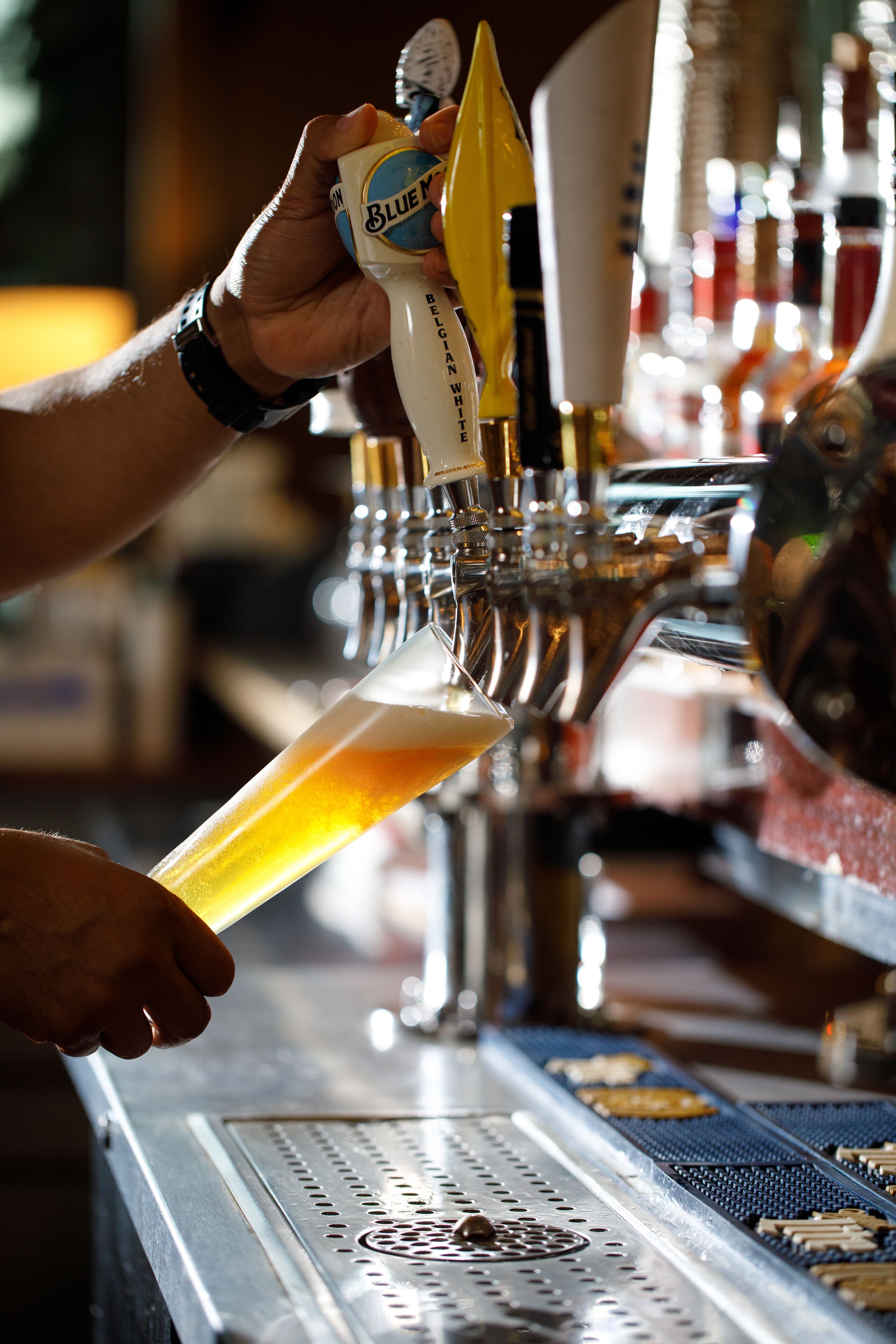 Uma mão servindo cerveja de uma torneira com a etiqueta 'Blue Moon' em um copo.