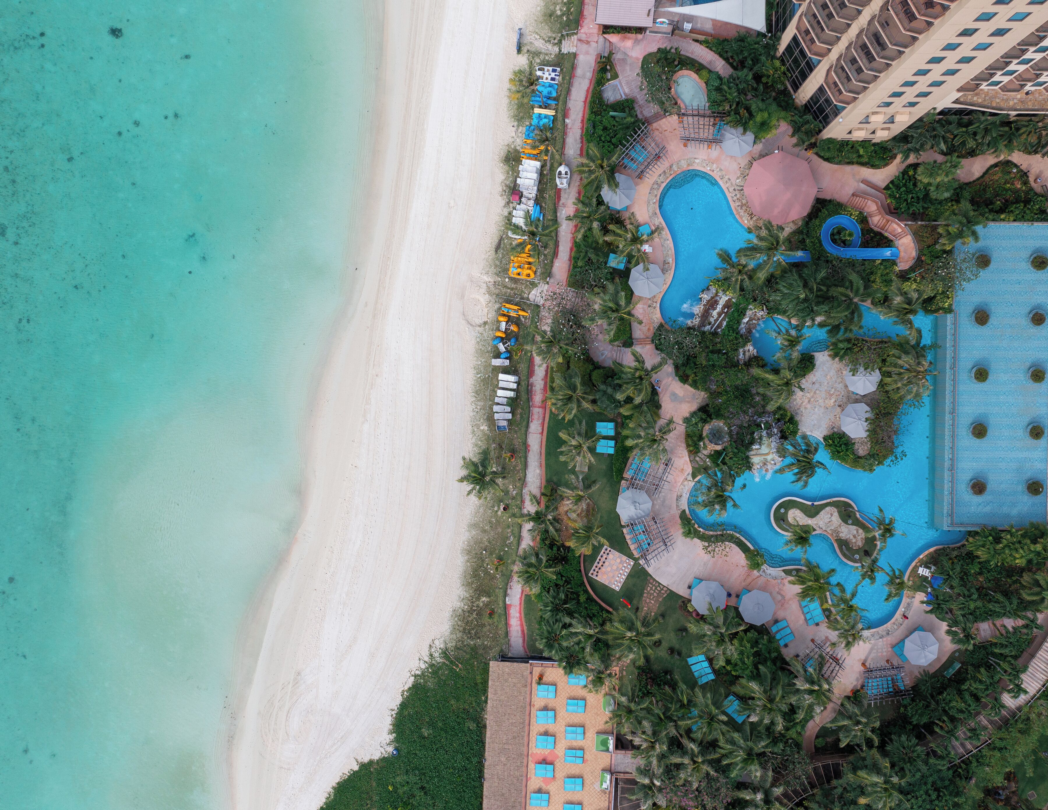 Vista aérea de um resort com praia, uma grande piscina e vários quartos de hóspedes.