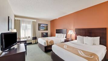 Quarto de hotel com duas camas, televisão, escrivaninha e janela com cortinas.