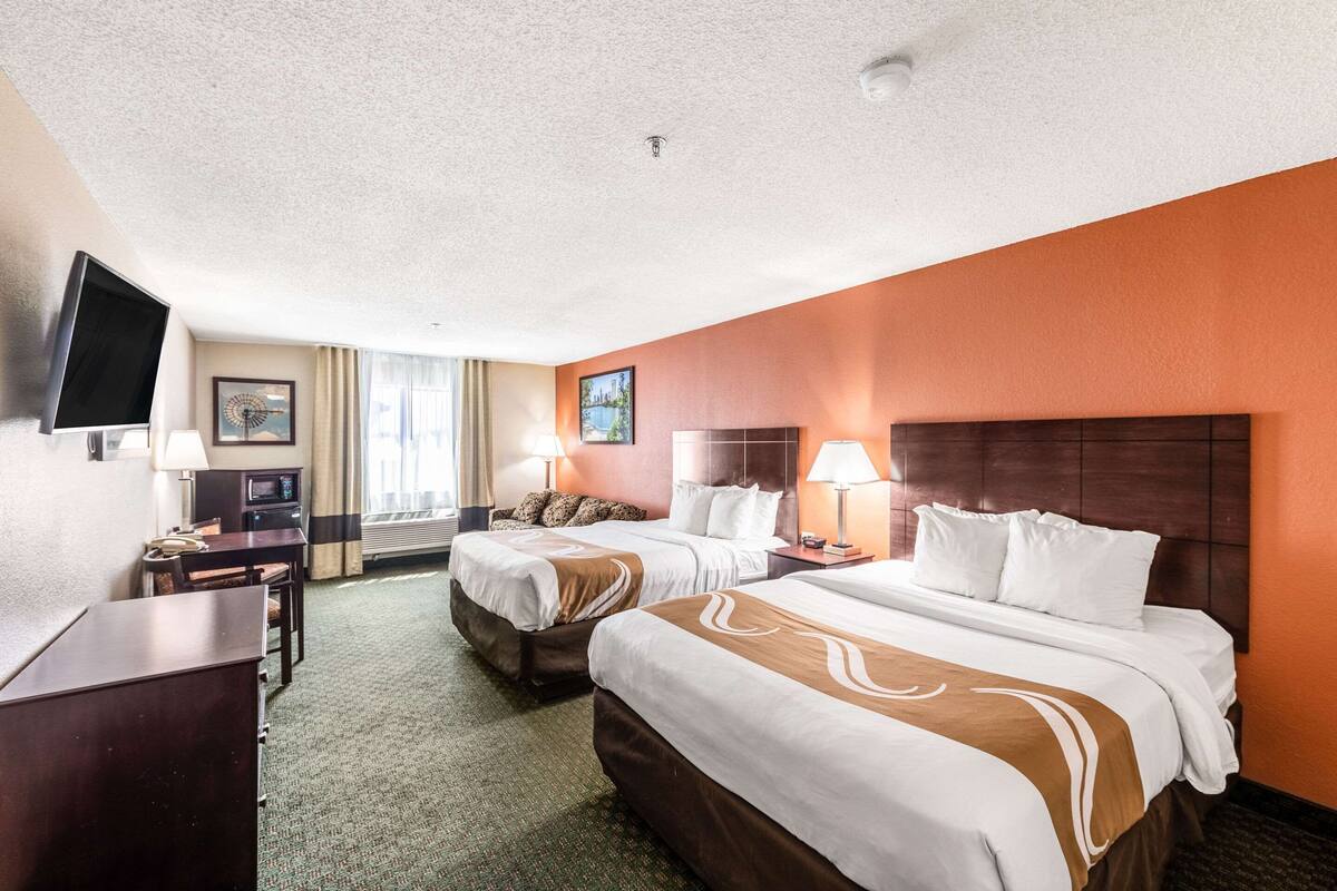 Quarto de hotel com duas camas, uma mesa de trabalho, televisão e janela com cortinas.