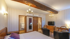 Quarto de hotel com uma cama grande, cabeceira de madeira, escrivaninha com cadeira, televisão e guarda-roupa com espelho.