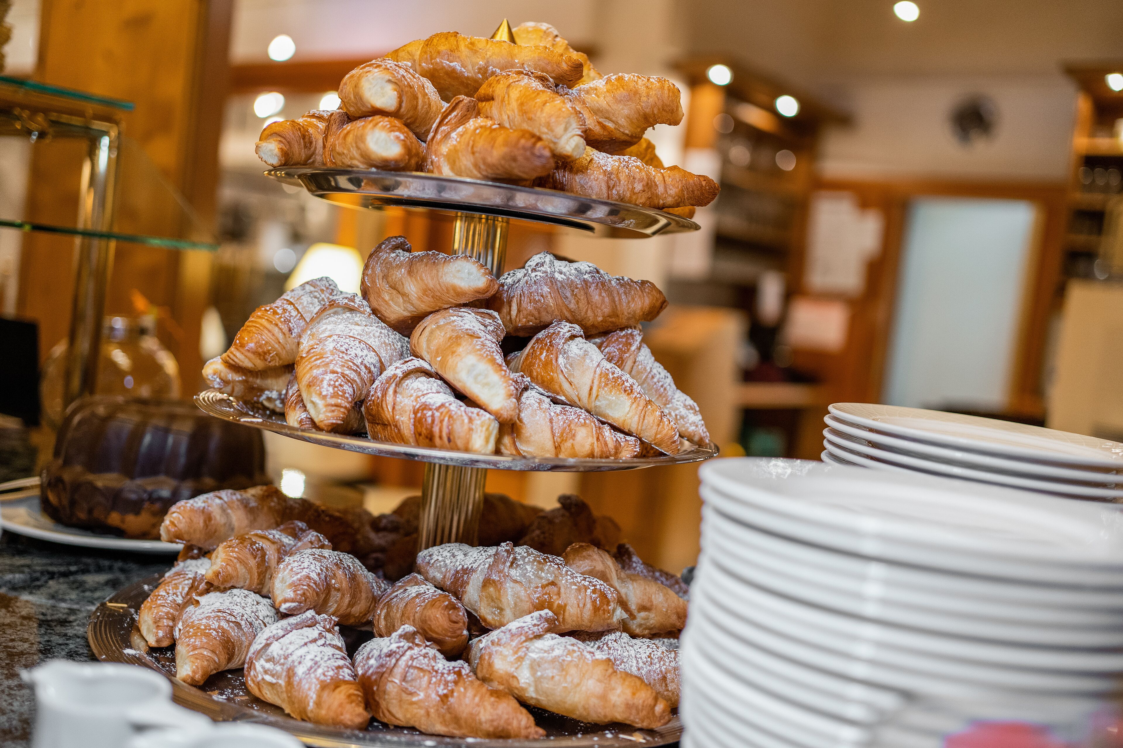 Exposição em vários níveis com uma variedade de doces, principalmente croissants, dispostos sobre um suporte de metal.