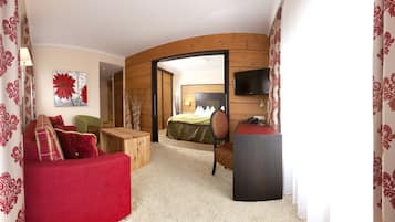 Quarto de hotel moderno com uma parede curva de madeira, uma cama com cabeceira verde, um sofá vermelho, uma escrivaninha e uma TV de tela plana na parede.