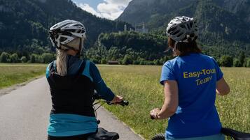 Dois ciclistas em um caminho pavimentado, com uma paisagem montanhosa ao fundo.