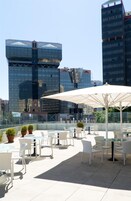Terraço no telhado com mobiliário de exterior, plantas em vasos e vista para edifícios modernos.
