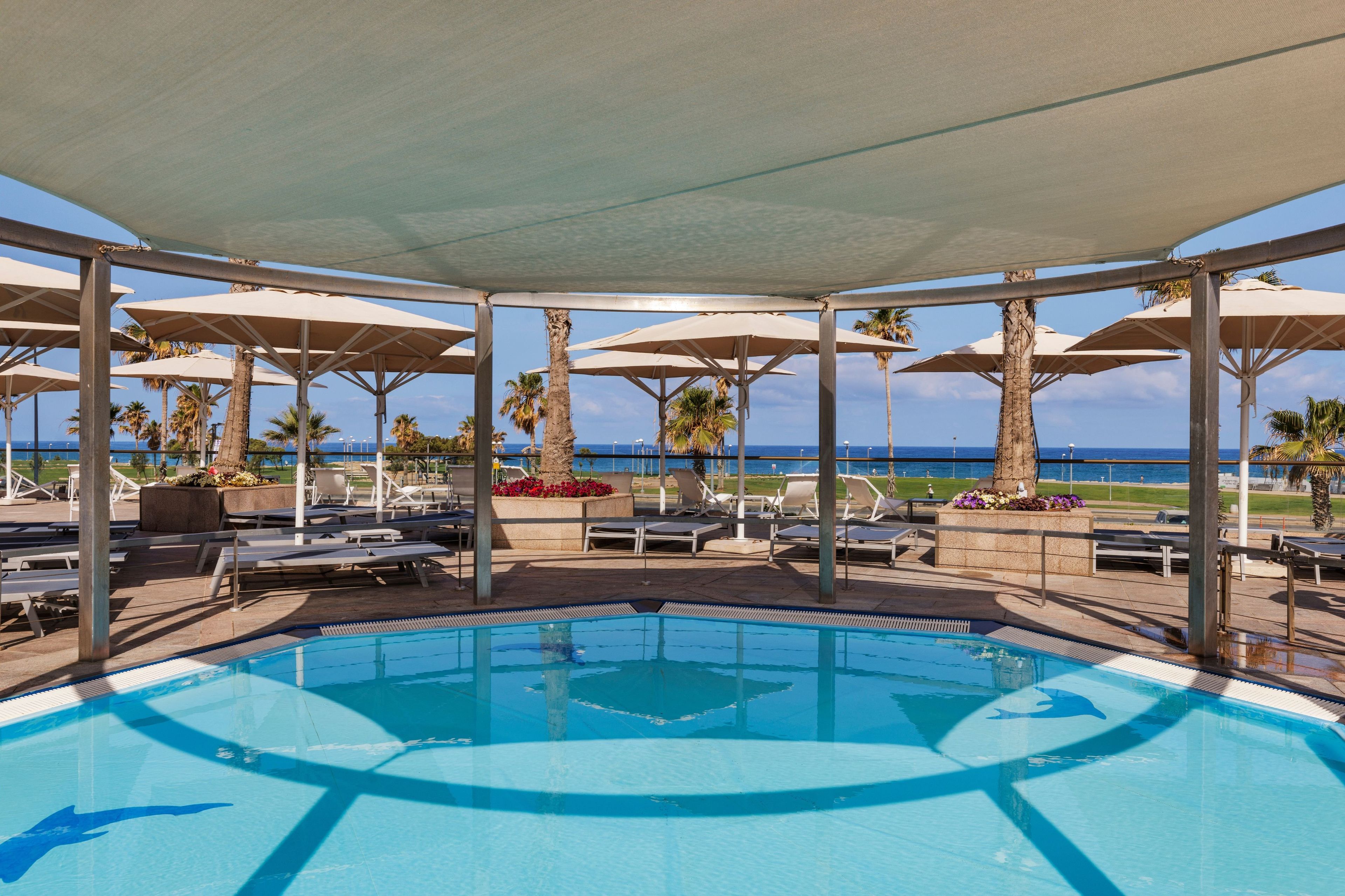 Área da piscina com guarda-sóis, espreguiçadeiras e vista para o mar.
