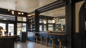 Uma área de bar com bancada de mármore, banquetas e adega.