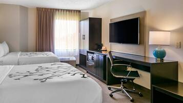 Quarto de hotel com duas camas, uma escrivaninha, uma cadeira, uma televisão e um abajur.
