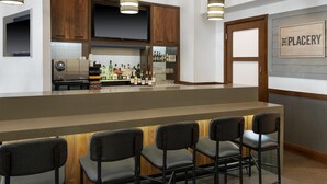 Uma área de bar com armários de madeira, um balcão com garrafas e uma placa com a inscrição THE PLACERY.