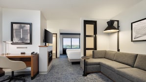Quarto de hotel com escrivaninha, cadeira, sofá, televisão e obras de arte.