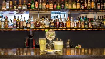 Um bar com diversas garrafas de bebidas e dois copos de coquetéis no balcão.