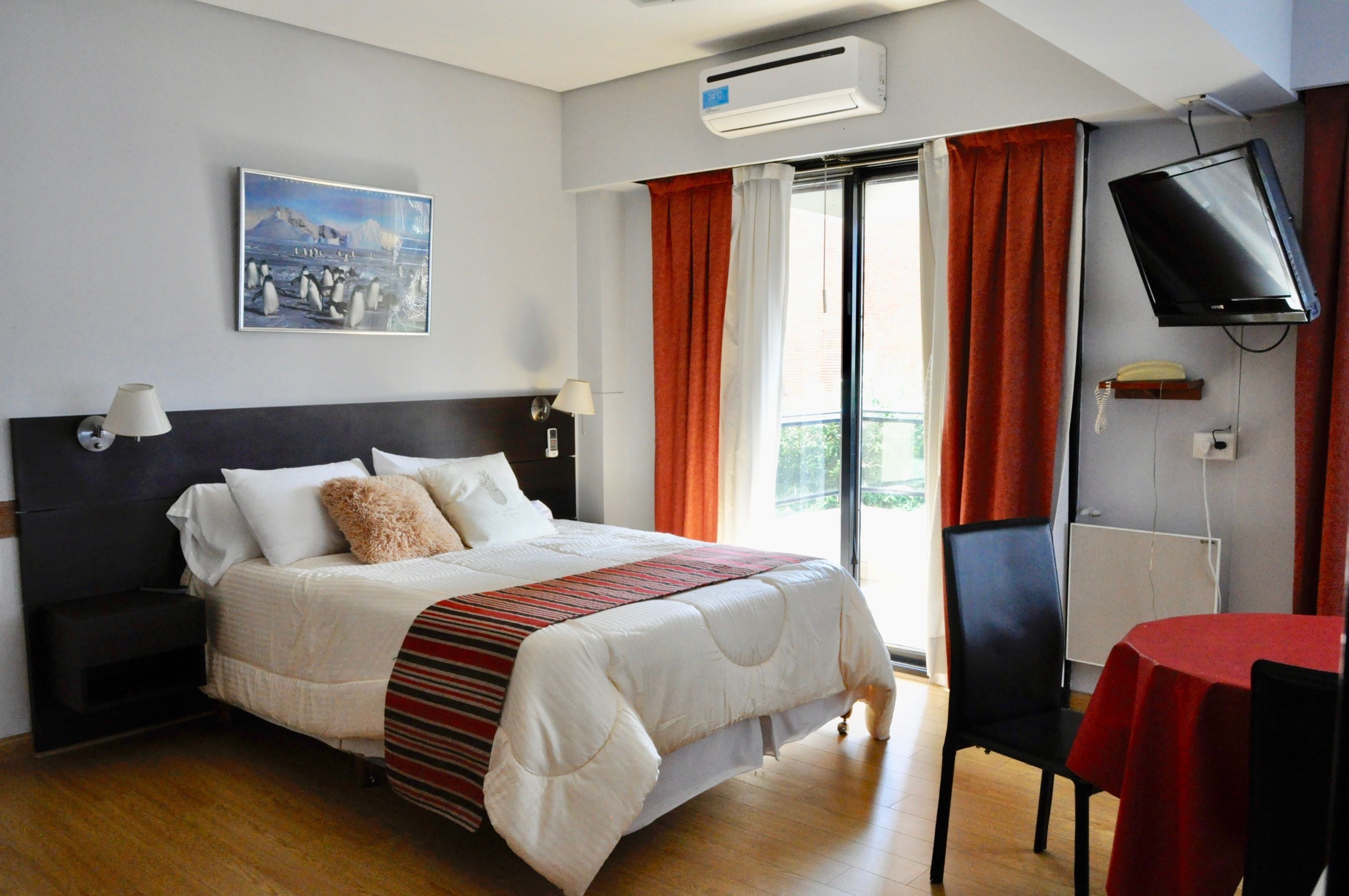 Quarto de hotel com cama, televisão, janela com cortinas e um quadro na parede.