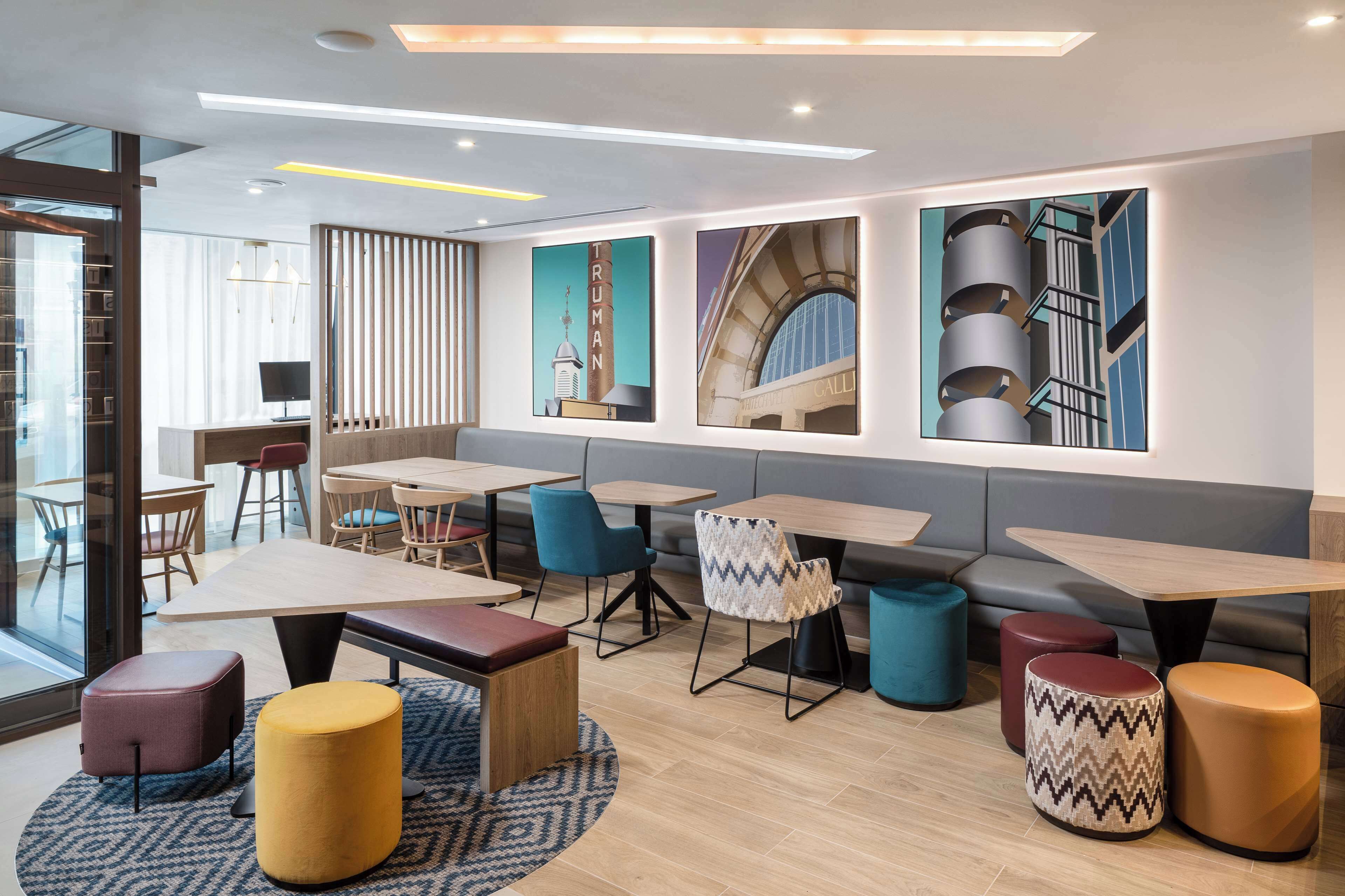 Um restaurante moderno com mesas e cadeiras de madeira, um tapete estampado e obras de arte nas paredes.