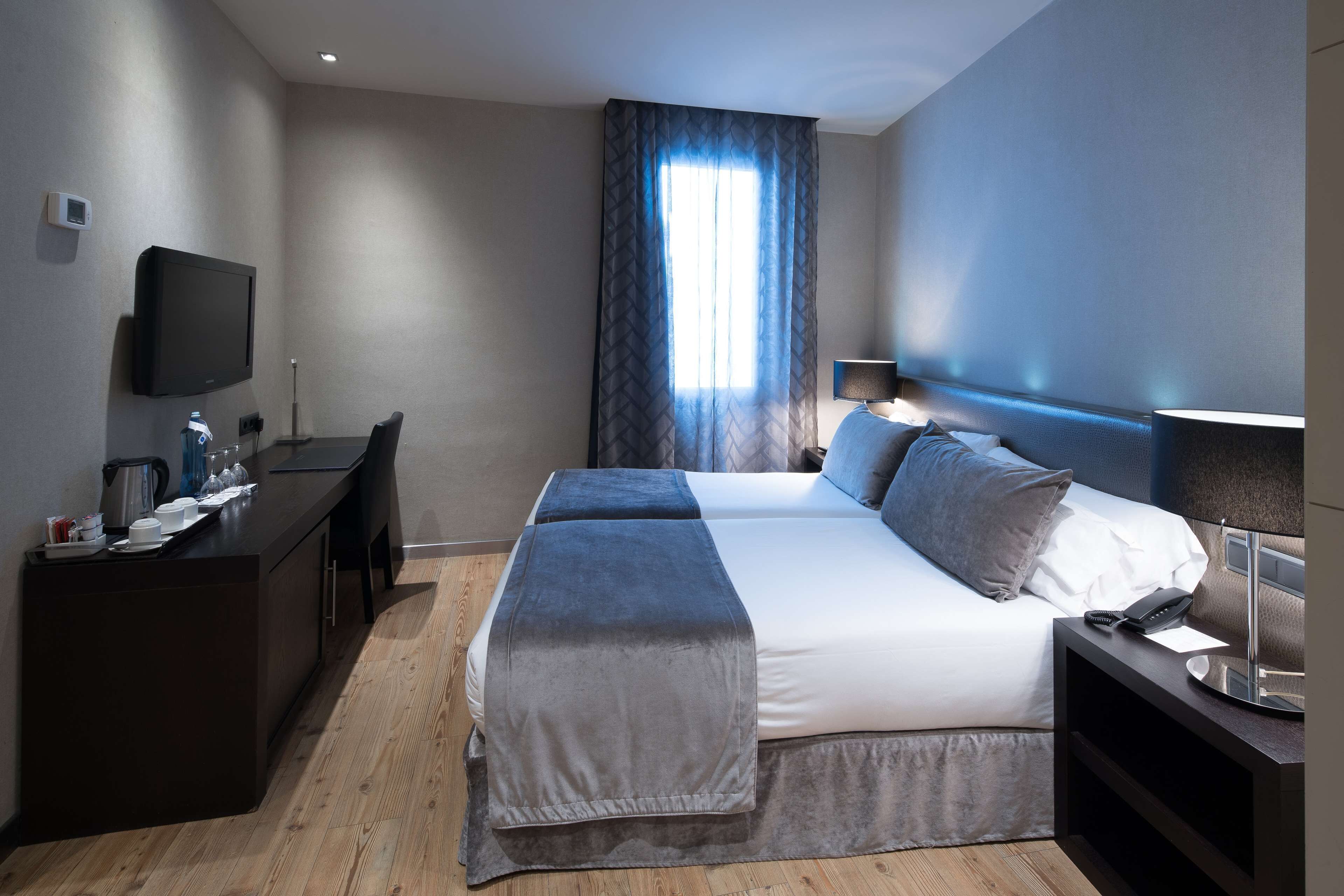 Quarto de hotel moderno com uma cama grande, uma escrivaninha, uma televisão de tela plana e uma janela com cortinas.