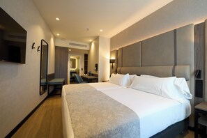 Quarto de hotel com uma cama grande, escrivaninha, cadeira, televisão e espelho.