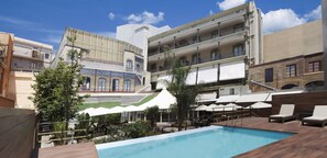 Área de piscina no terraço com espreguiçadeiras, guarda-sóis e vista para os edifícios ao redor.