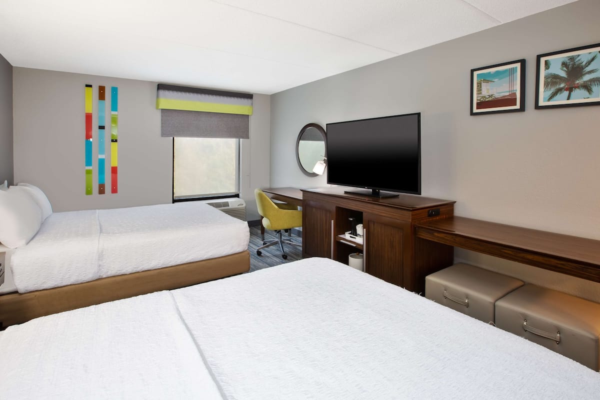 Quarto de hotel com duas camas, uma escrivaninha, uma televisão e uma cadeira.