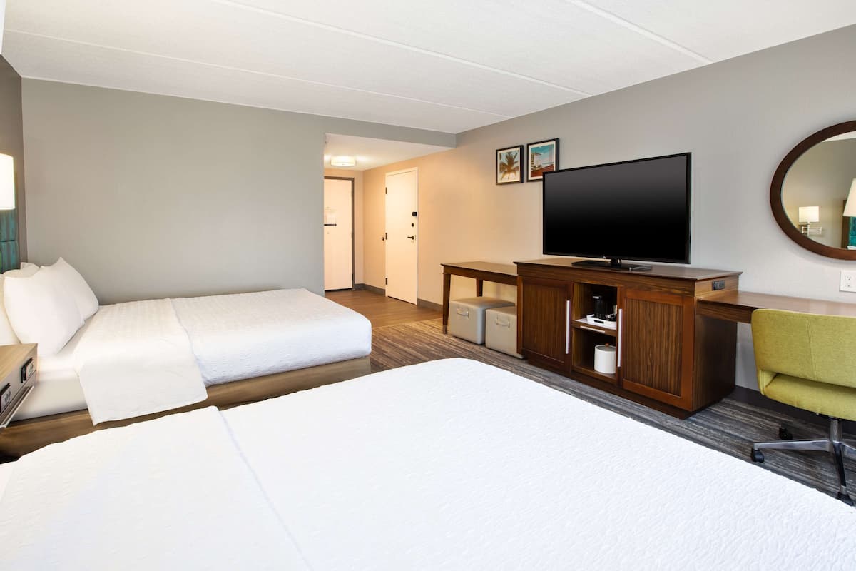Quarto de hotel com uma cama grande, uma escrivaninha com televisão, uma cadeira e uma pequena mesa.