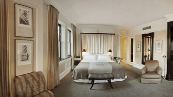 Quarto de hotel com uma cama grande, uma cadeira, um banco e quadros nas paredes.