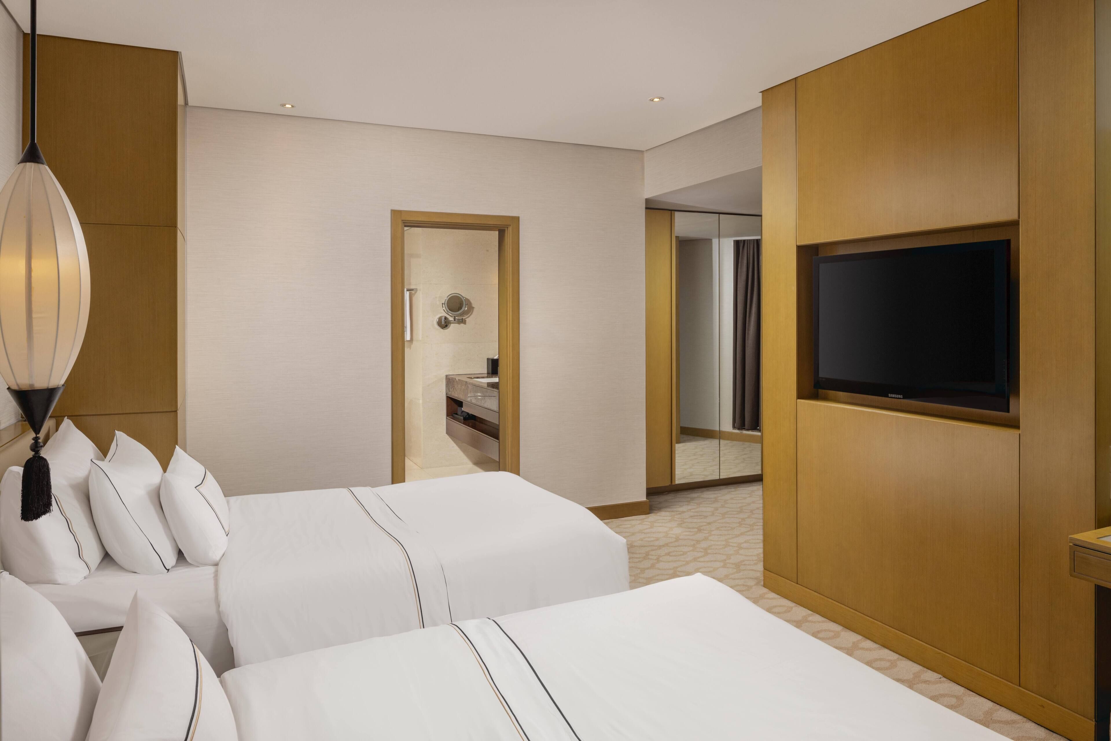 Quarto de hotel com duas camas, uma televisão, um espelho e uma porta para o banheiro.