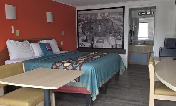 Quarto de hotel com cama, mesa, cadeira, janela grande e vista para a paisagem urbana.
