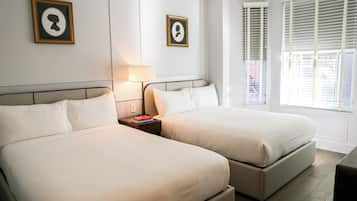 Quarto de hotel com duas camas, uma mesa de cabeceira com abajur e quadros nas paredes.