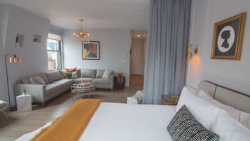 Quarto de hotel moderno com uma cama grande, um sofá, uma mesa de centro e um candelabro.