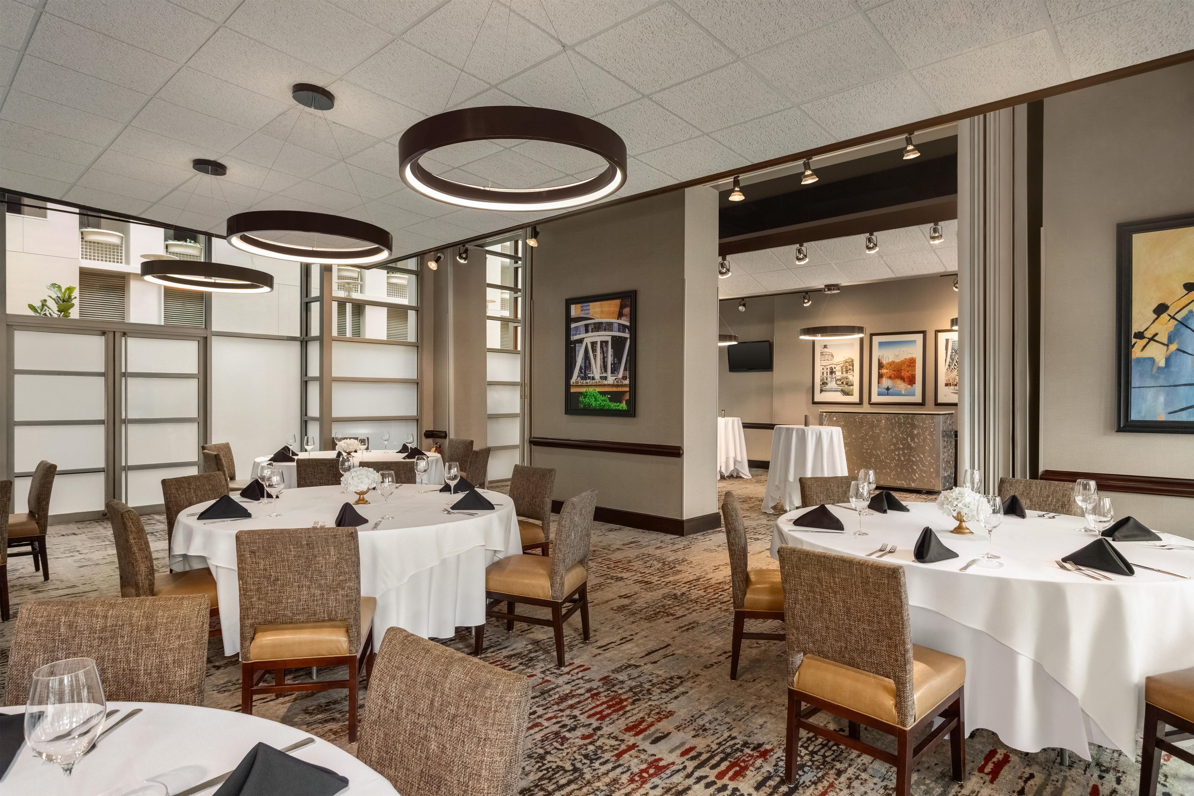 Uma área de refeições de hotel com mesas redondas, cadeiras e luminárias modernas.