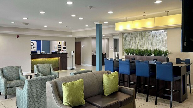 Um hall de hotel moderno com balcão de recepção, área de estar com sofás e cadeiras, e um bar com banquetas.