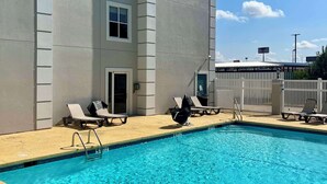 Piscina com espreguiçadeiras e porta que dá para um edifício.