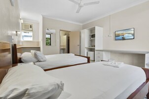 Quarto de hotel com duas camas, televisão, ventoinha no teto e banheiro visível por uma porta aberta.