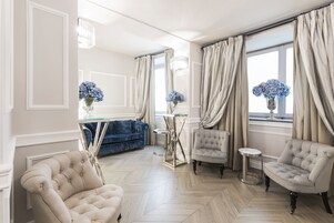 Uma sala de estar ampla, com piso em padrão herringbone, um sofá azul e duas poltronas.