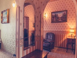 Quarto com papel de parede estampado, um quadro emoldurado, uma cadeira, uma mesa e um abajur.