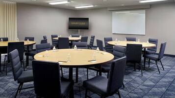 Uma sala de conferências com várias mesas e cadeiras, um ecrã grande e um projetor.