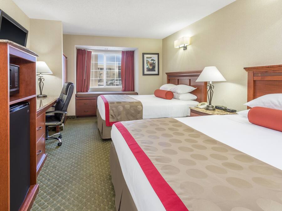 Quarto de hotel com duas camas, uma mesa de trabalho com computador, uma cadeira e uma televisão.