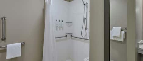 Uma casa de banho moderna com chuveiro, sanita e barras de apoio.